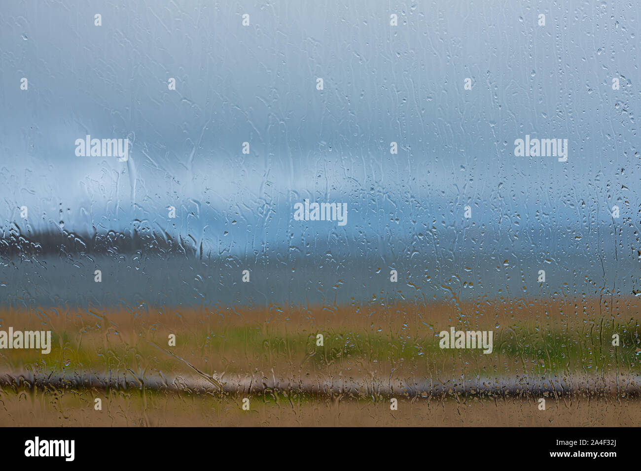Rain drops on a large panoramic window looking out to sea on a stormy ...