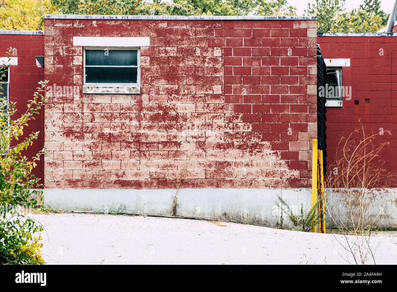 Faded red brick building with leaves over grown on an overcast day ...