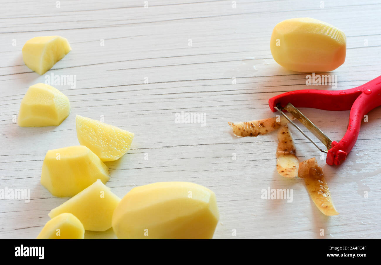 Peeled potatoes on a white, wooden table with grey lines. With tool to ...