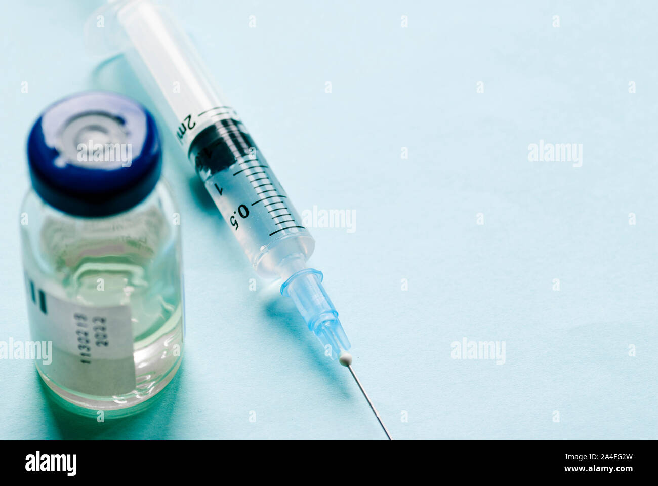 Opened vial of vaccine medication and full syringe on white table ...