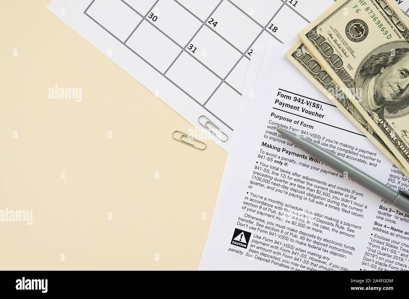 IRS Form 941-V Payment Voucher blank lies with pen and many hundred dollar bills on calendar ...