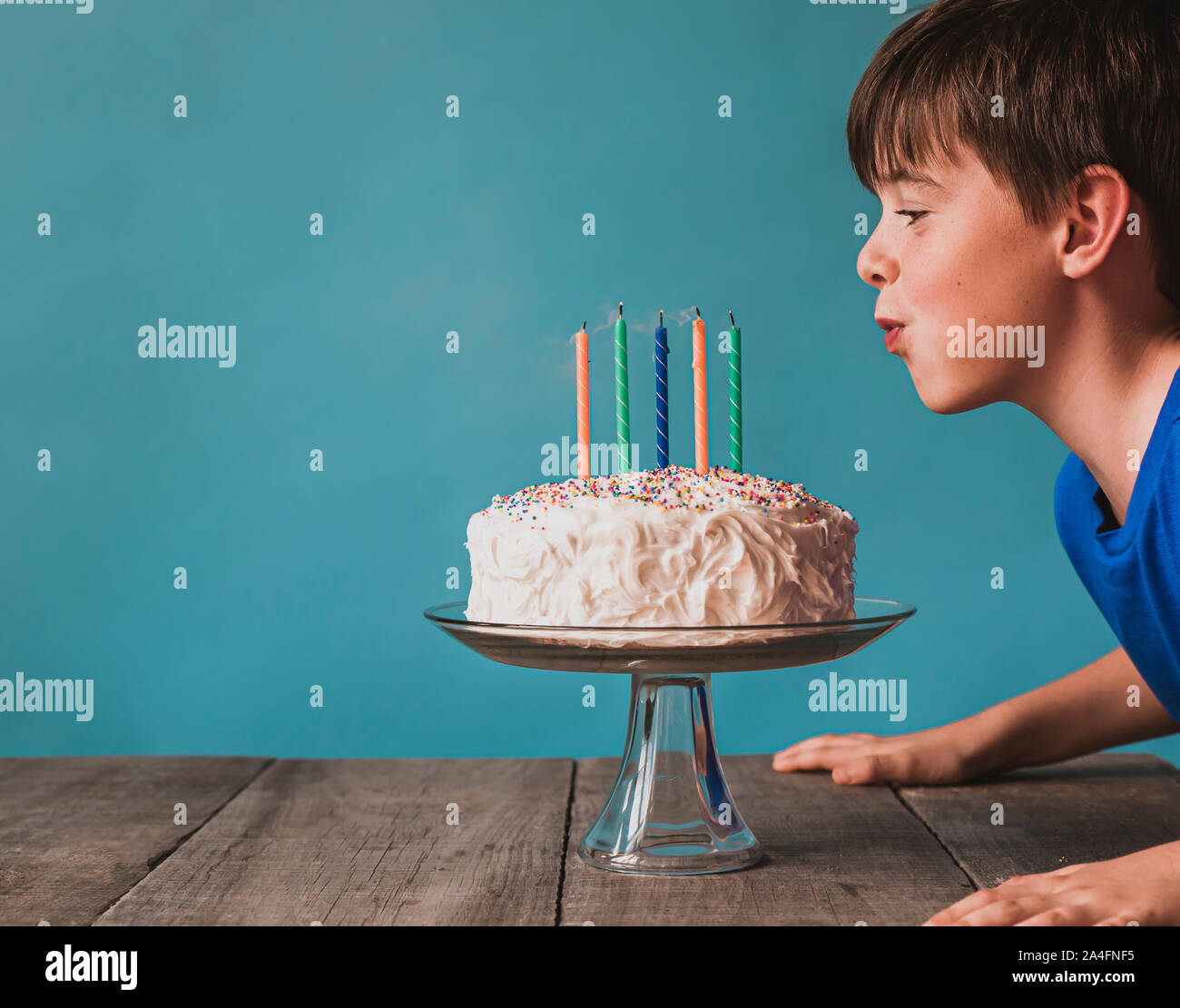 Boy blowing out candles on a birthday cake against blue background ...