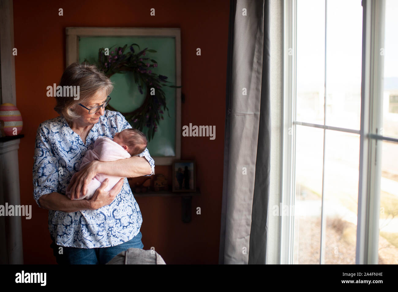 Grandmother holding newborn granddaughter by window at home Stock Photo ...