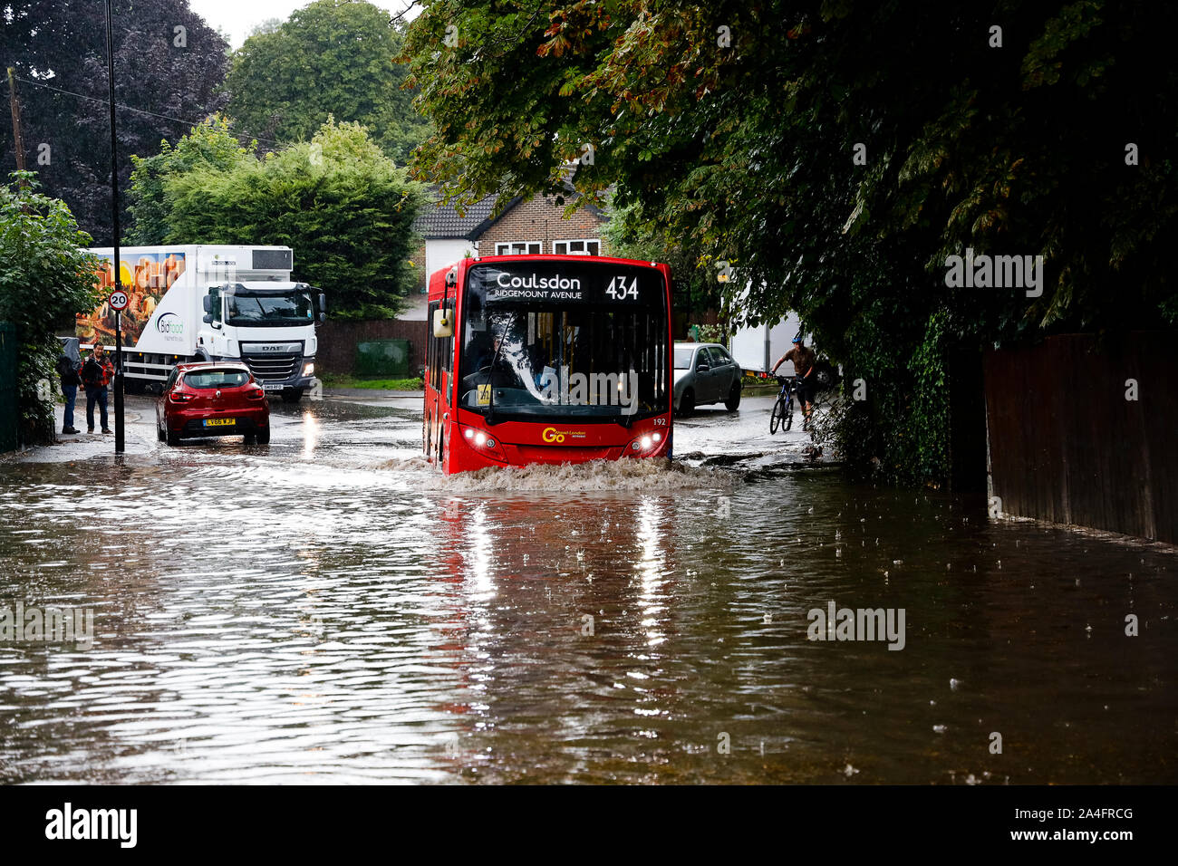 London, UK. A red bus splashes through flood water in Kenley, south ...