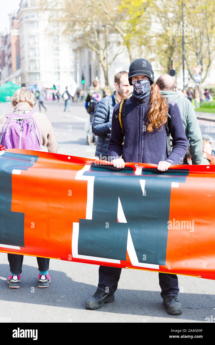 London, UK. A protester wearing a skeleton face mask holds a banner as ...