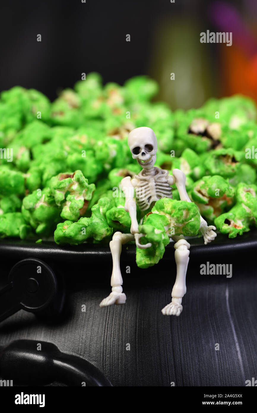 A skeleton sits on the edge of a cauldron and holds in its hands a ...
