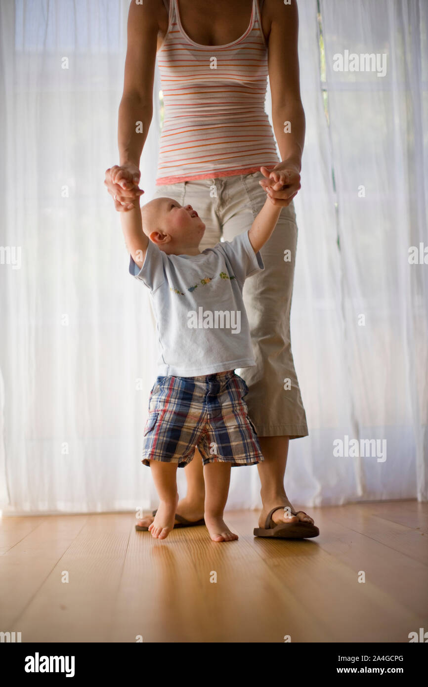 Mother helping baby son to take his first steps Stock Photo - Alamy
