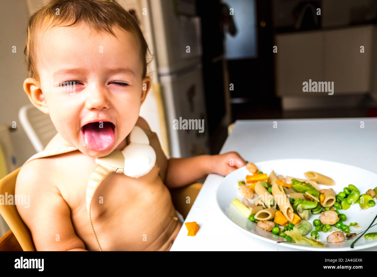 Baby with funny face enjoying his food eating with his hands making a ...