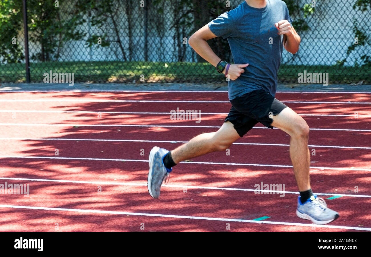 A high school track and field runner is running fast on a red track in ...