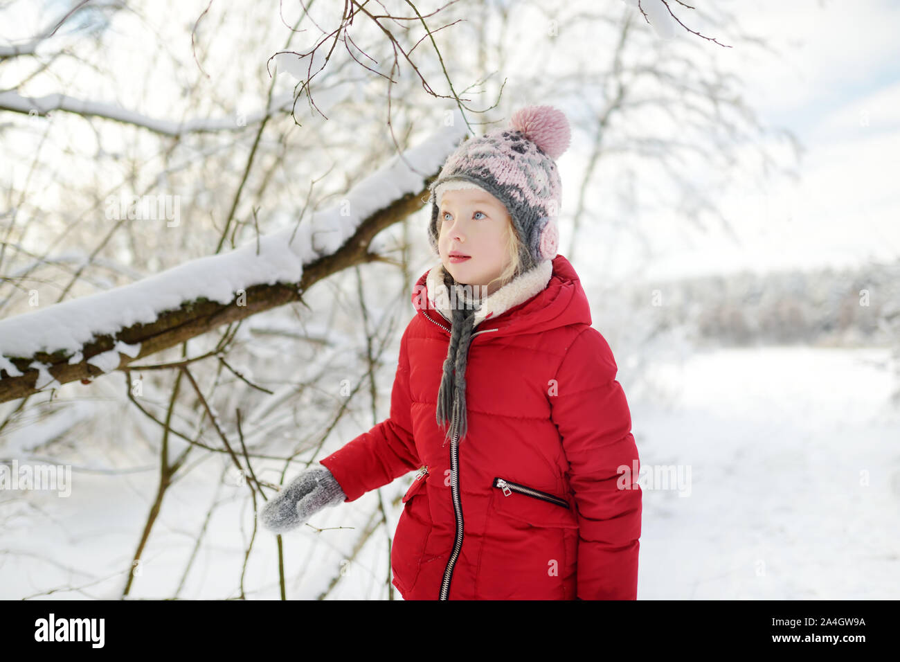 Adorable young girl having fun in beautiful winter park during snowfall ...