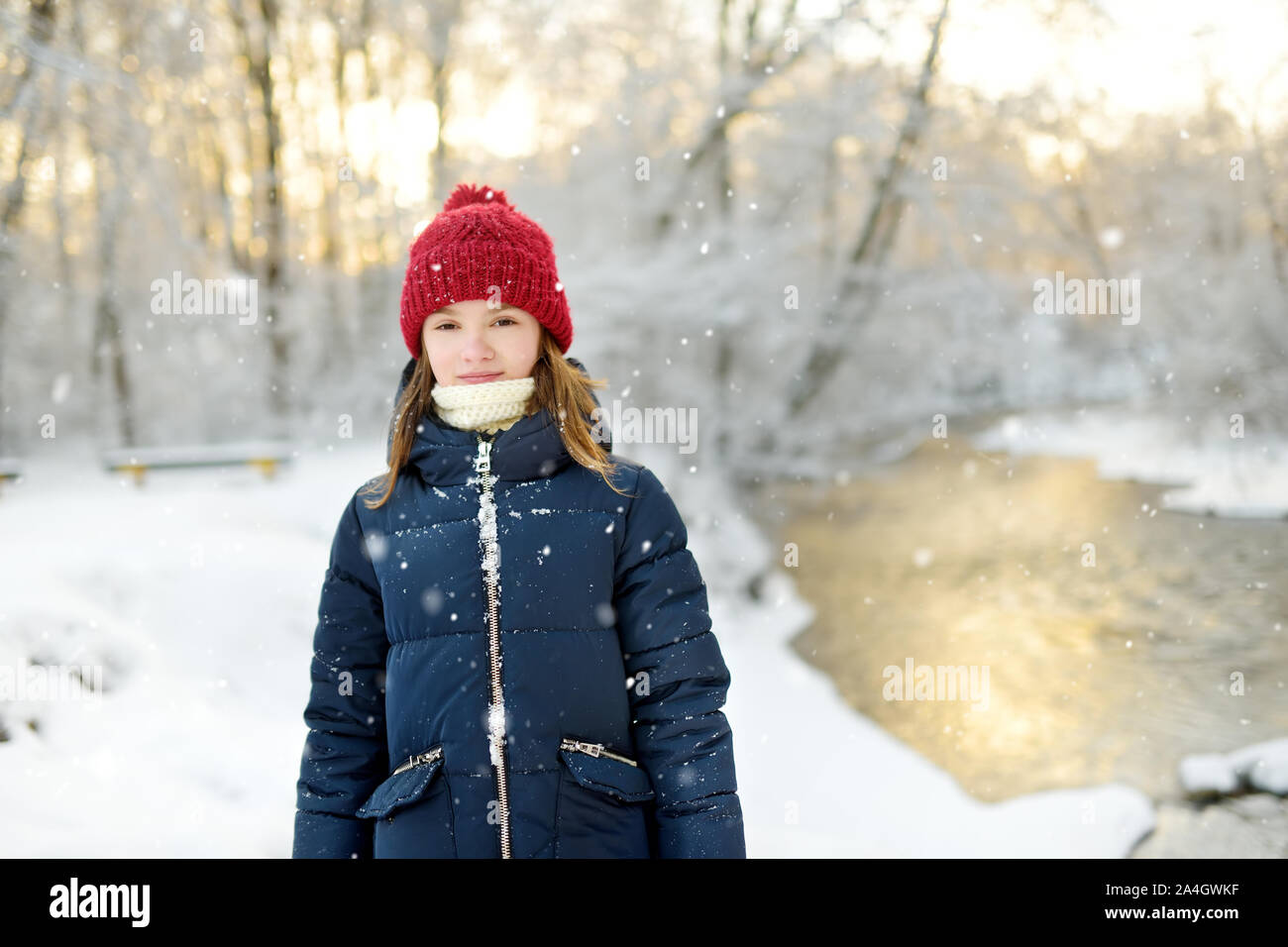 Adorable young girl having fun in beautiful winter park during snowfall ...