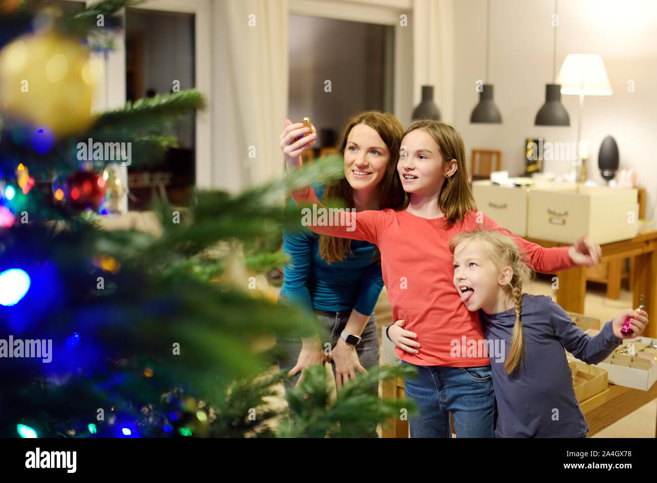 Family of three decorating the Christmas tree together on Christmas eve ...