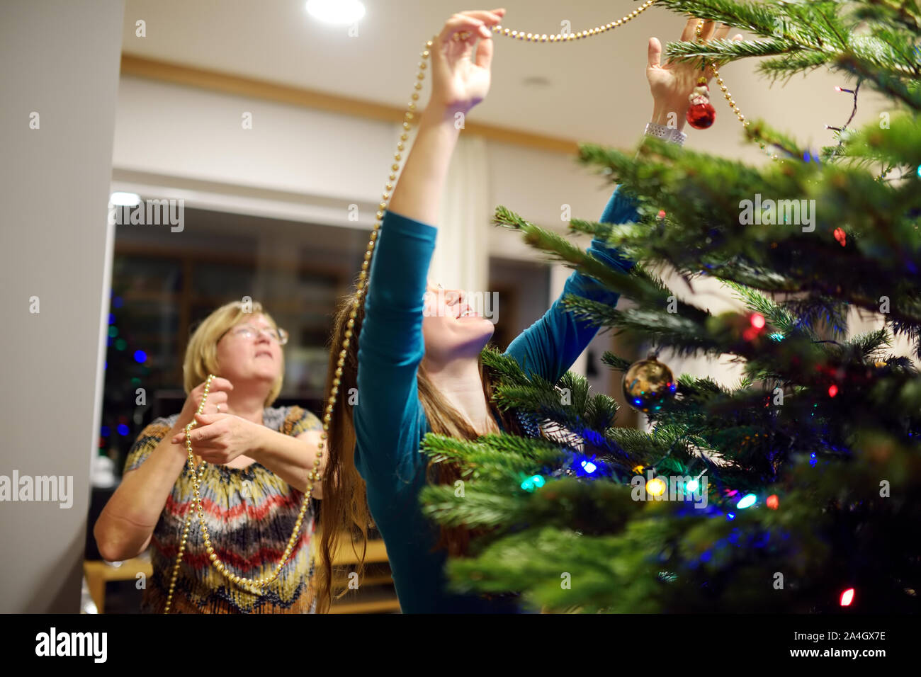 Family decorating the Christmas tree with golden garland. Trimming the ...