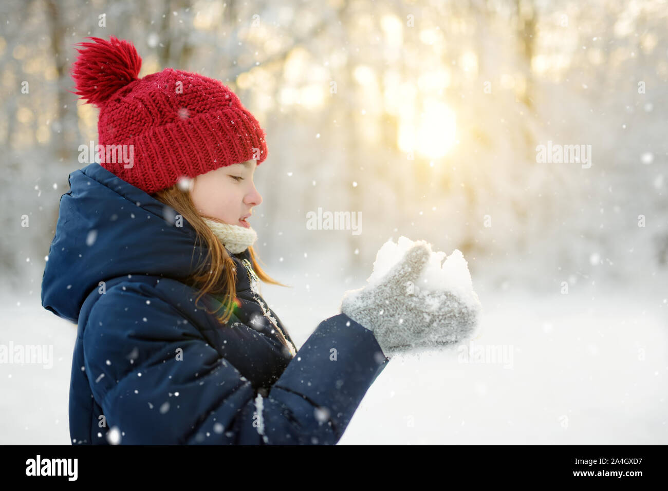 Adorable young girl having fun in beautiful winter park during snowfall ...