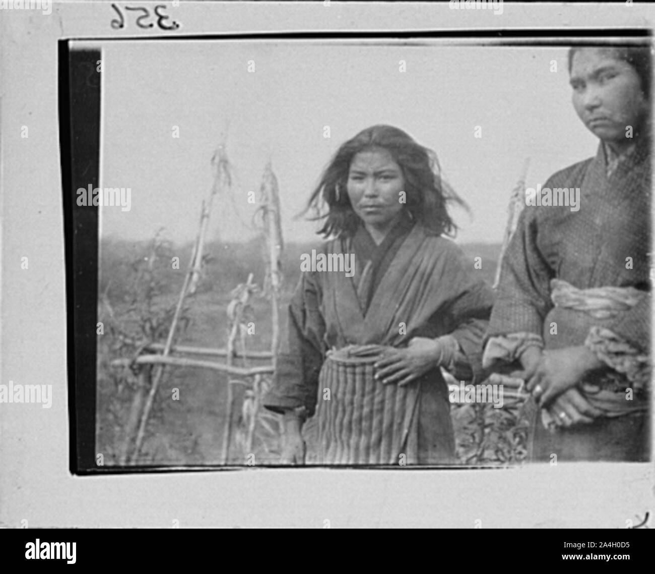 Two Ainu women standing outside in front of a pole fence Stock Photo ...
