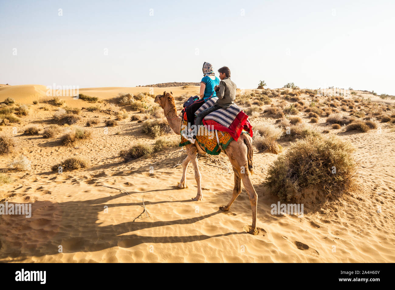 A female traveler and her camel guide riding a camel in the sand dunes ...