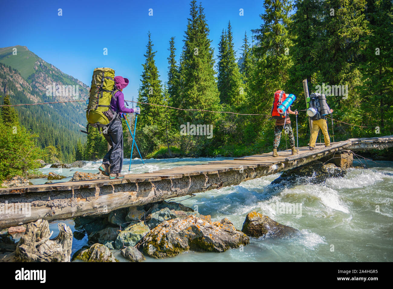 Hikers crossing over wood bridge under mountain river Stock Photo - Alamy