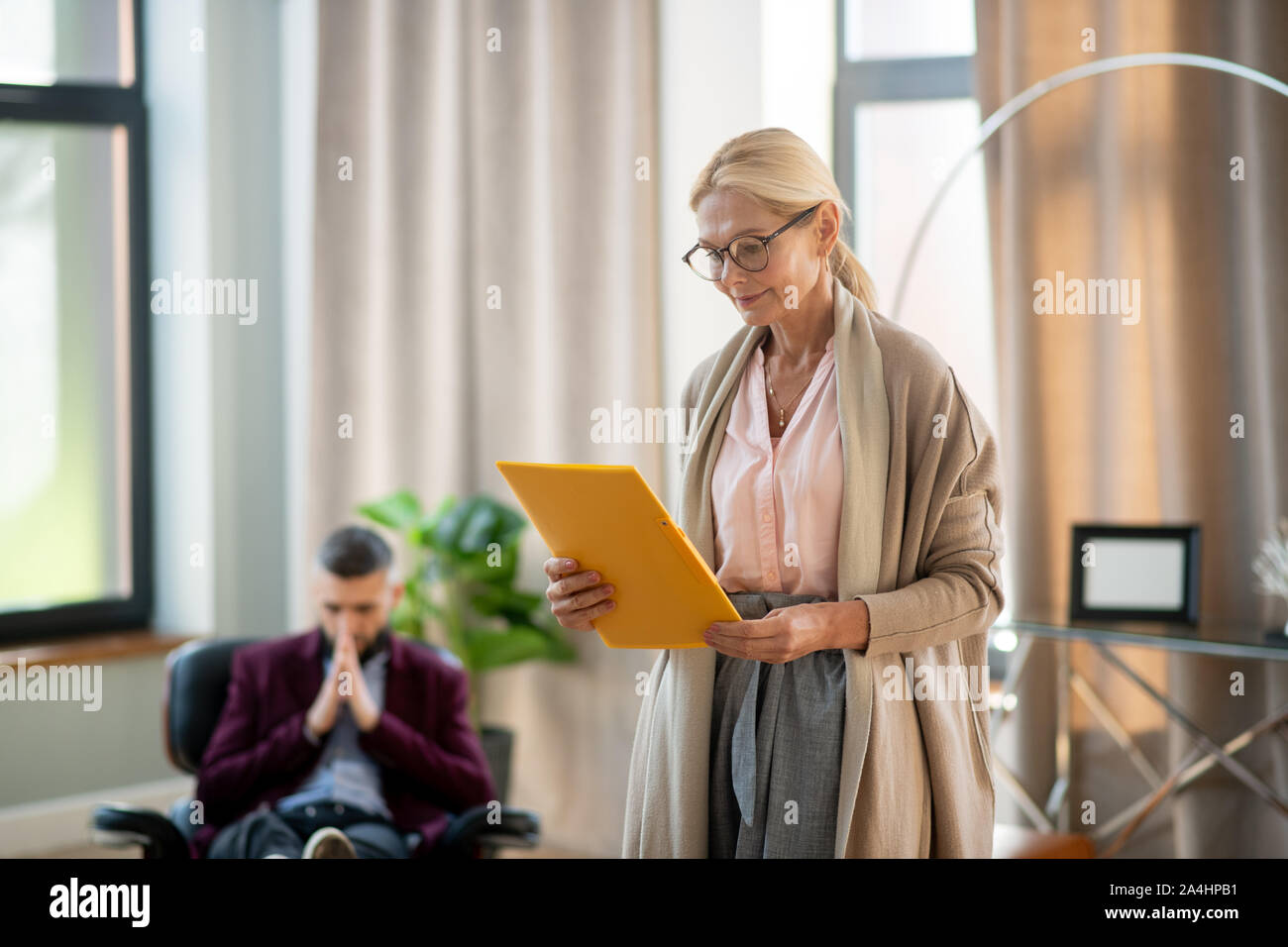 Blonde psychoanalyst wearing glasses reading info about patient Stock ...