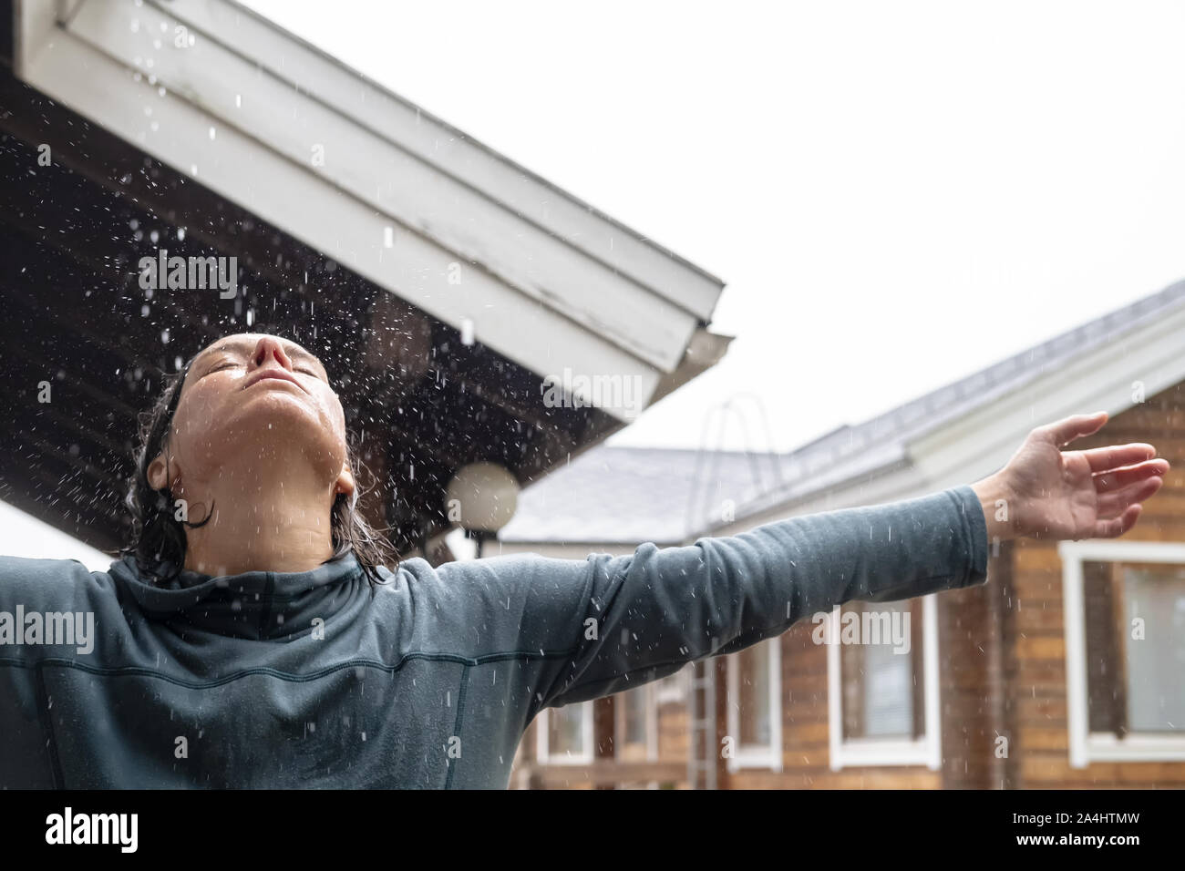 Woman spread her arms to the side and enjoys the heavy rain, tilting ...