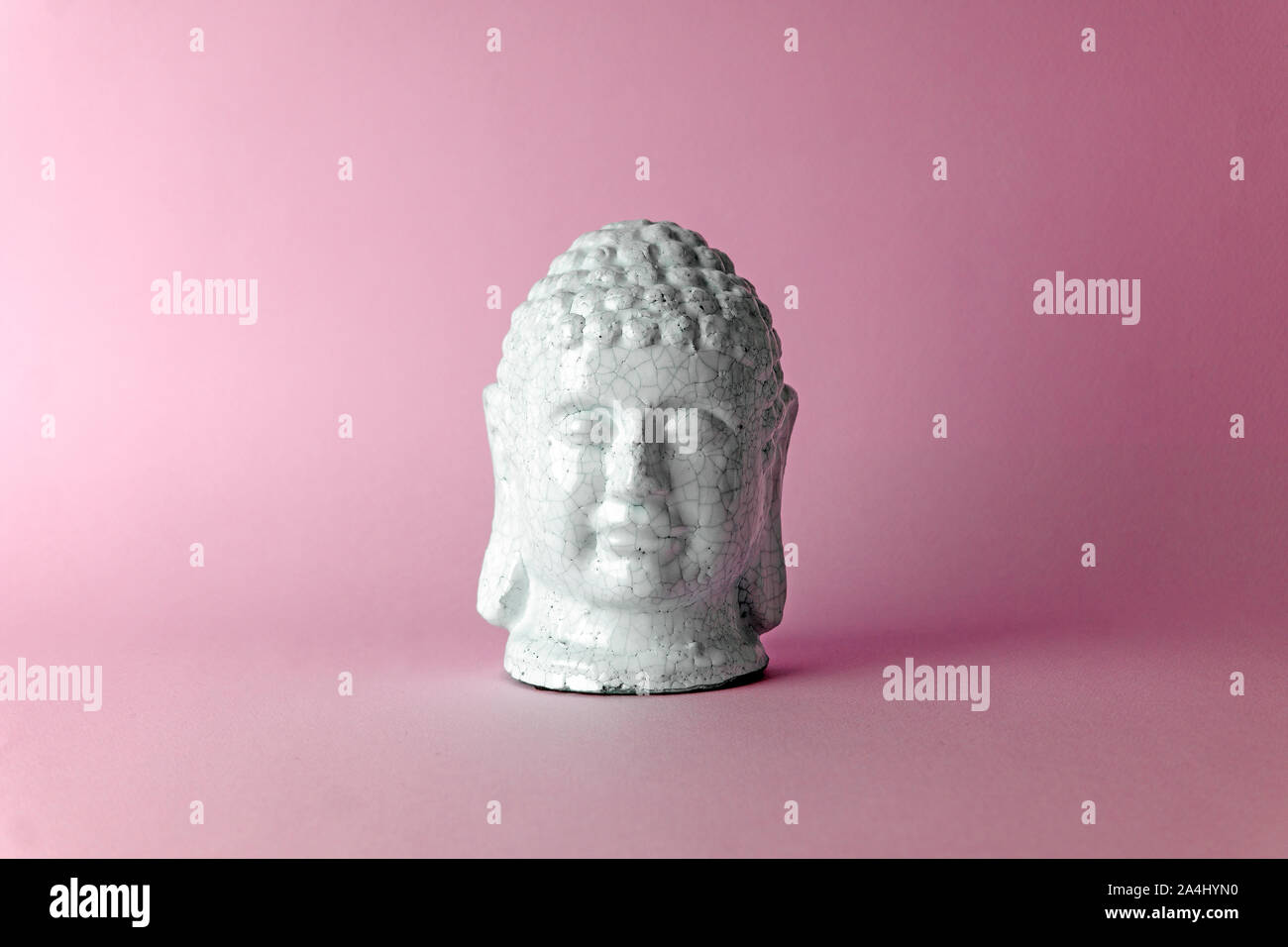 Ceramic head of a Buddha on a pink background. Minimal concept, copy ...