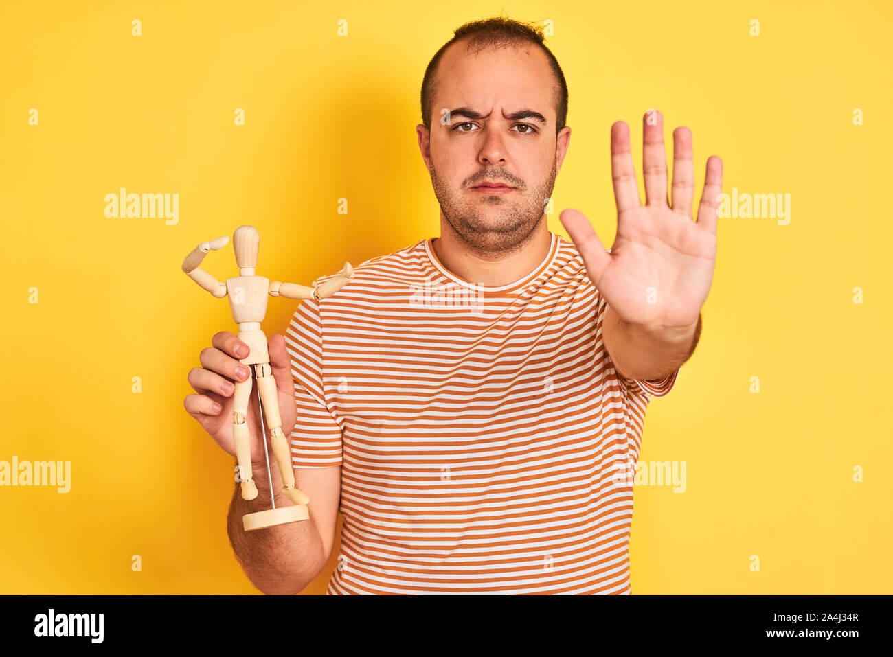 Young man holding figure of art dummy standing over isolated yellow ...