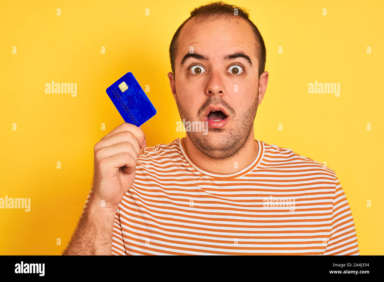 Young man holding blue credit card standing over isolated yellow ...