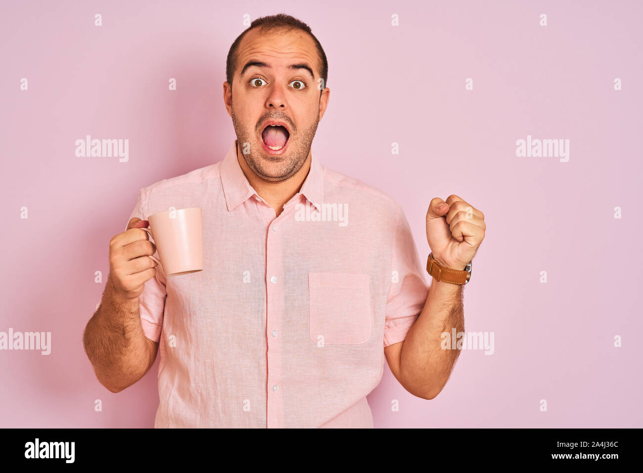 Young man drinking cup of coffee standing over isolated pink background ...