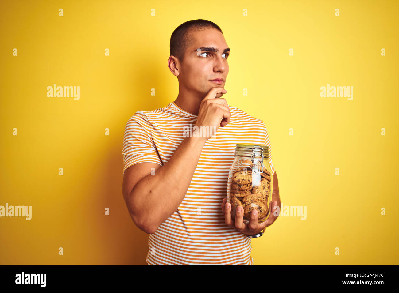 Young handsome man holding a jar of cookies over yellow isolated ...