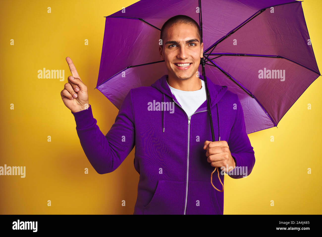 Young handsome man wearing purple umbrella over yellow isolated ...