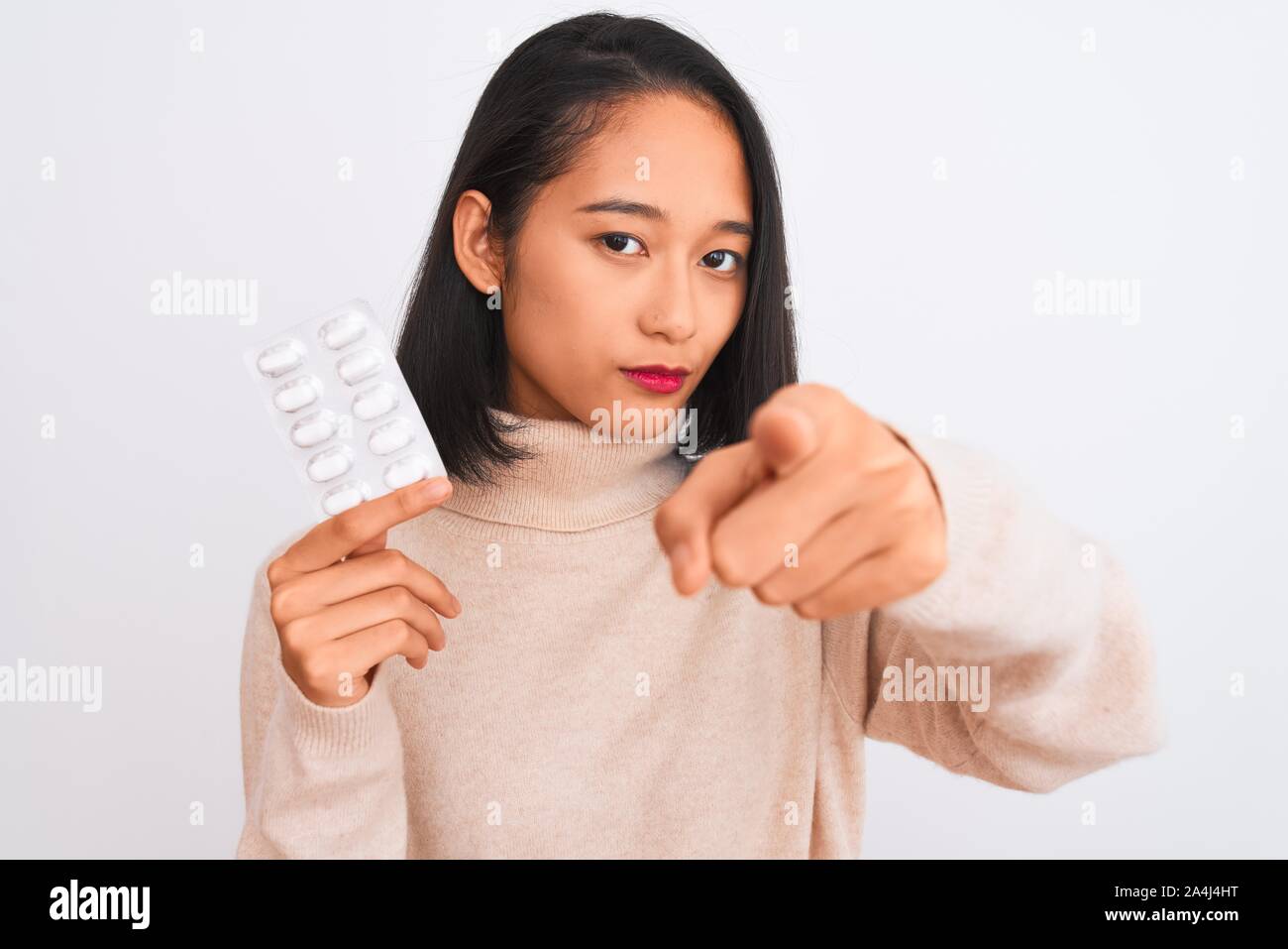 Young beautiful chinese woman holding pills standing over isolated ...