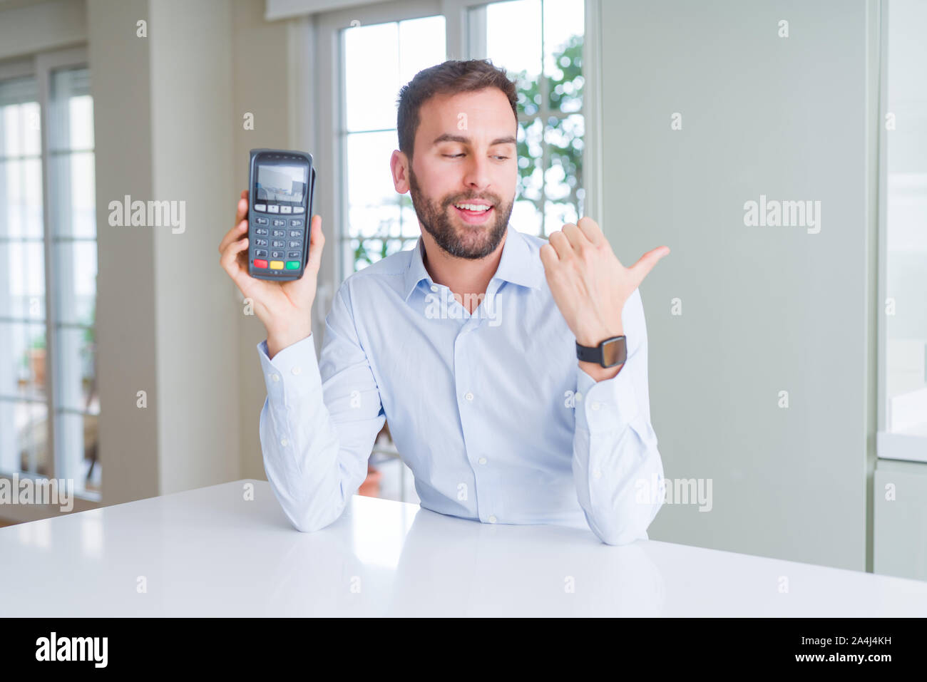 Handsome young man holding point of sale terminal pointing and showing ...