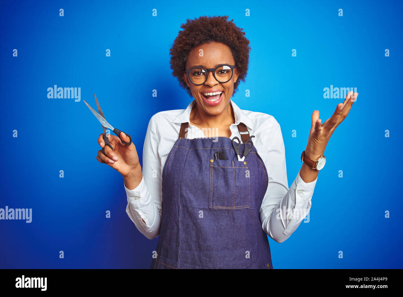 African american hairdresser woman holding scissors over blue isolated ...