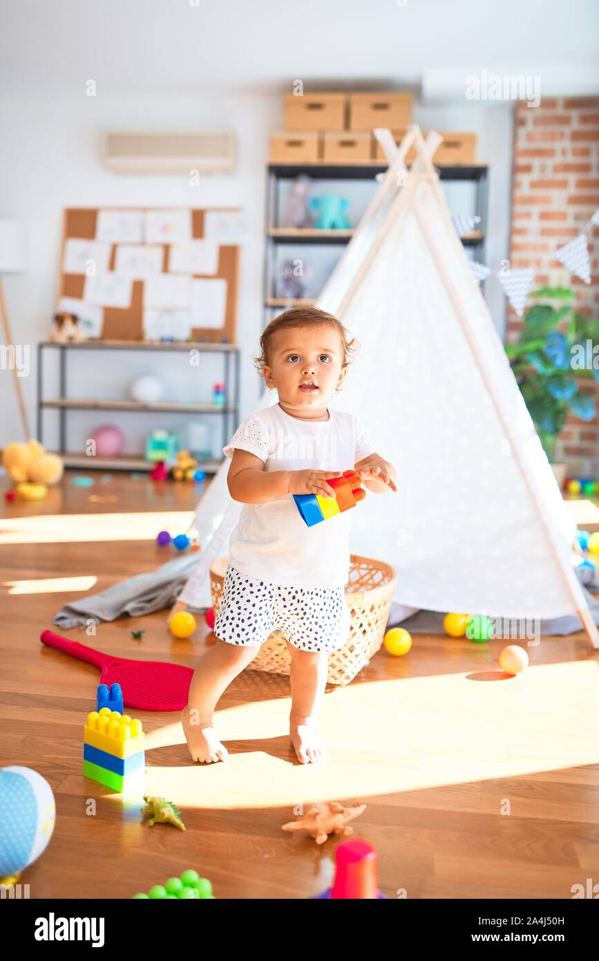 Adorable toddler playing with building blocks around lots of toys at ...
