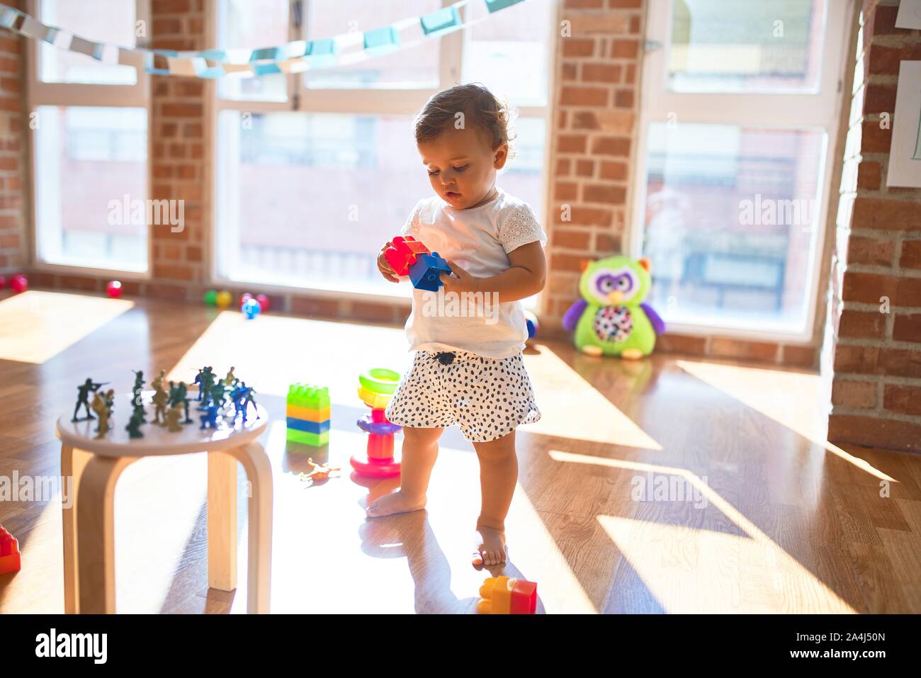 Adorable toddler playing with building blocks around lots of toys at ...