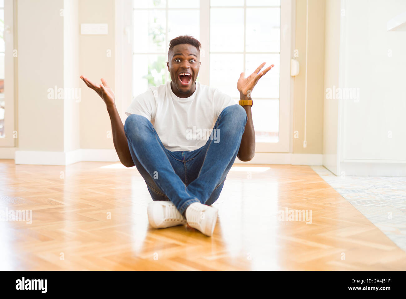 Handsome african american man sitting on the floor at home celebrating ...