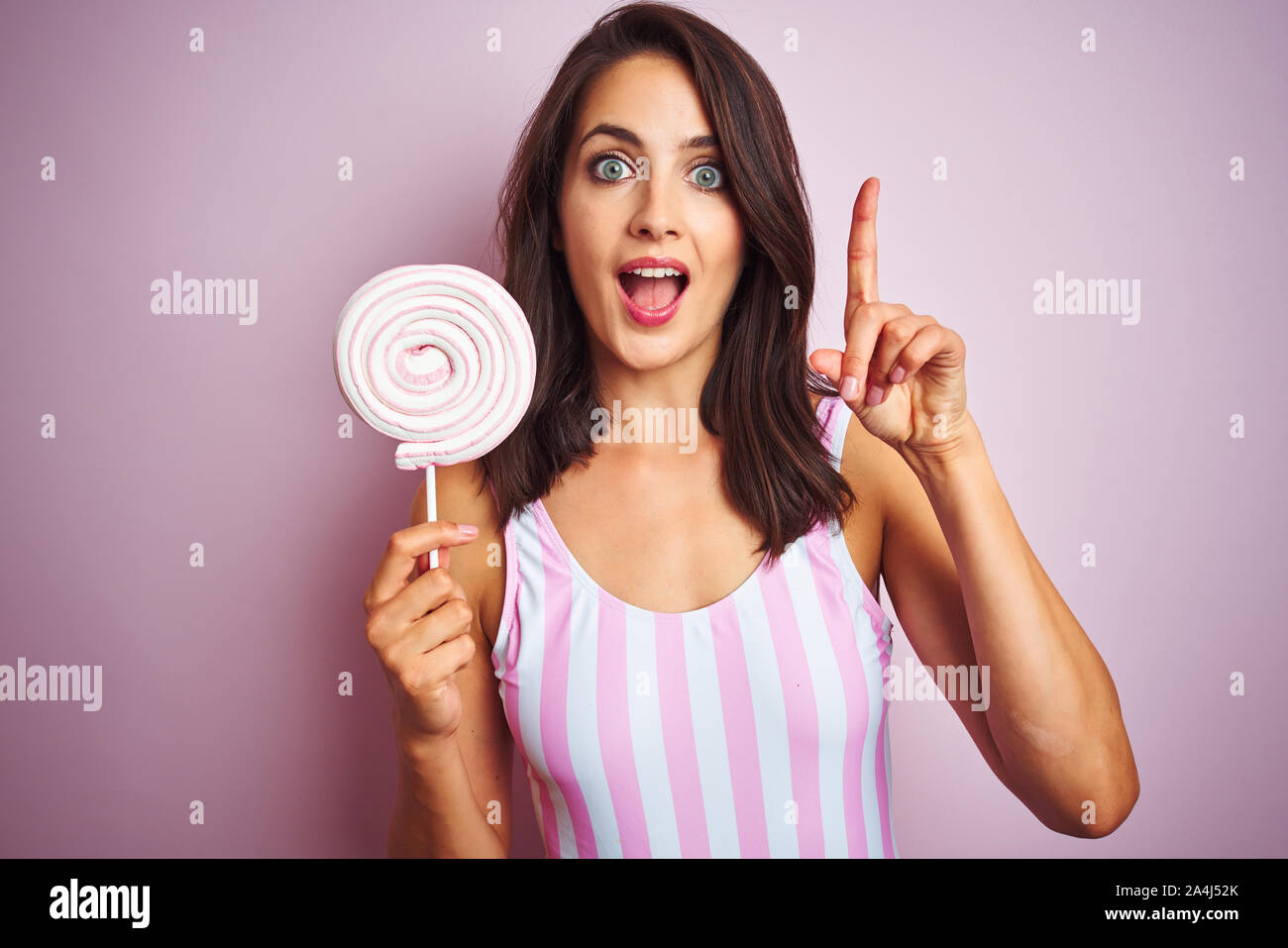 Young beautiful woman eating sweet candy over pink isolated background ...