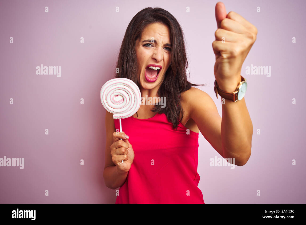 Young beautiful woman eating sweet candy over pink isolated background ...