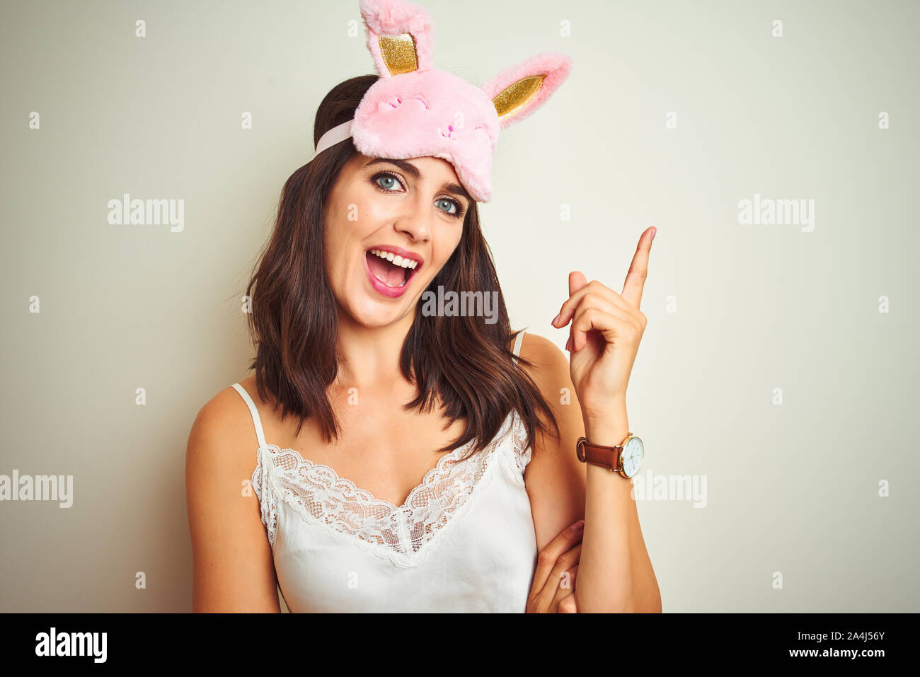 Young beautiful woman wearing pajama and mask standing over white ...