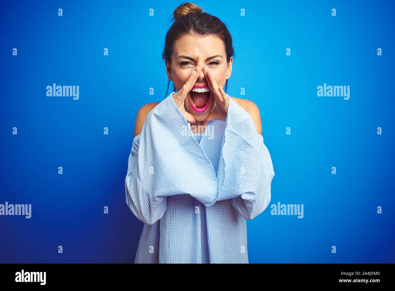 Young beautiful woman wearing bun hairstyle over blue isolated ...
