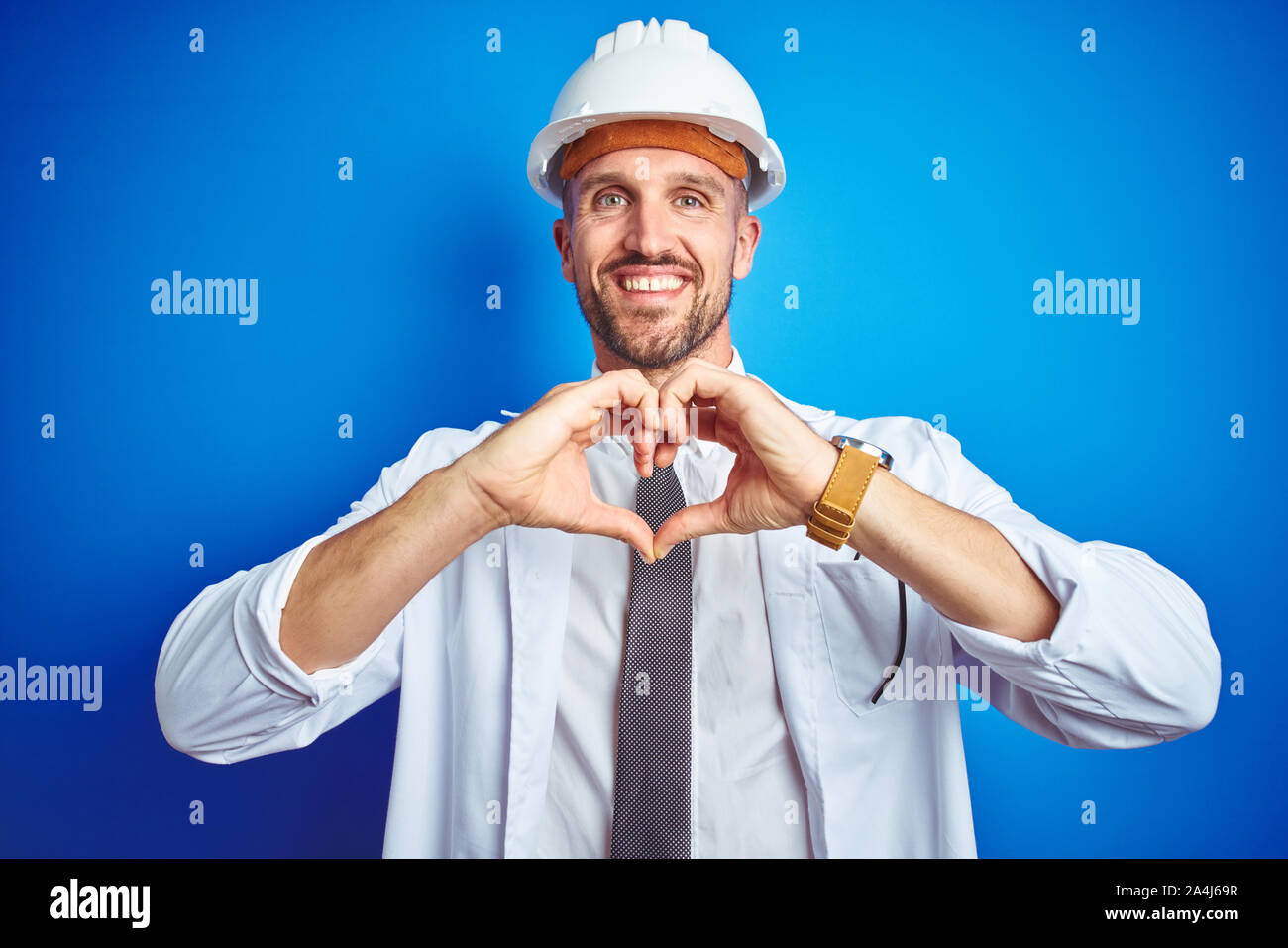 Young handsome engineer man wearing safety helmet over blue isolated ...