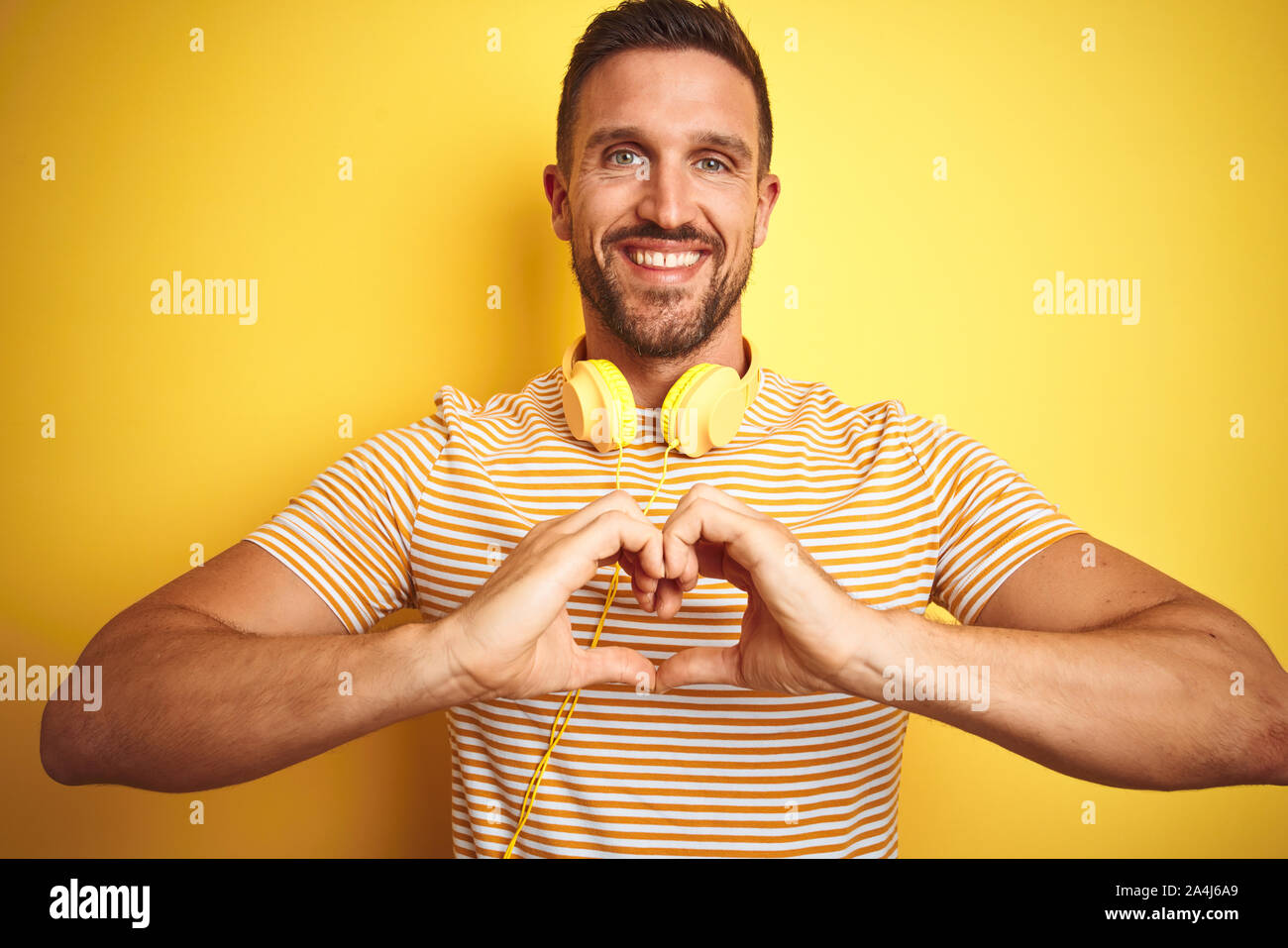 Young handsome man wearing headphones listening to music over yellow isolated background smiling ...