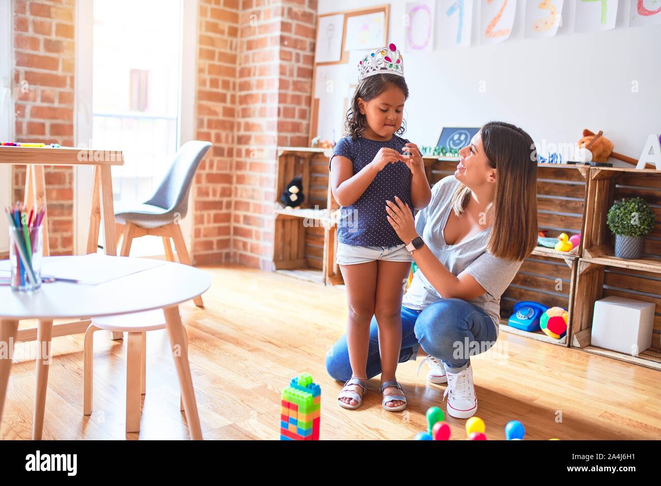 Beautiful teacher looking at toddler girl wearing princess crown at ...