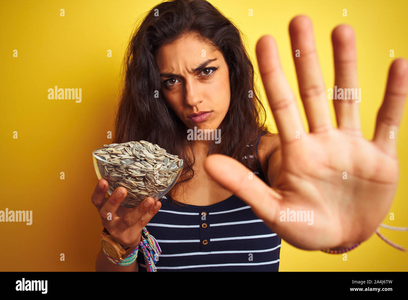 Young beautiful woman holding bowl with sunflowers seeds over isolated ...