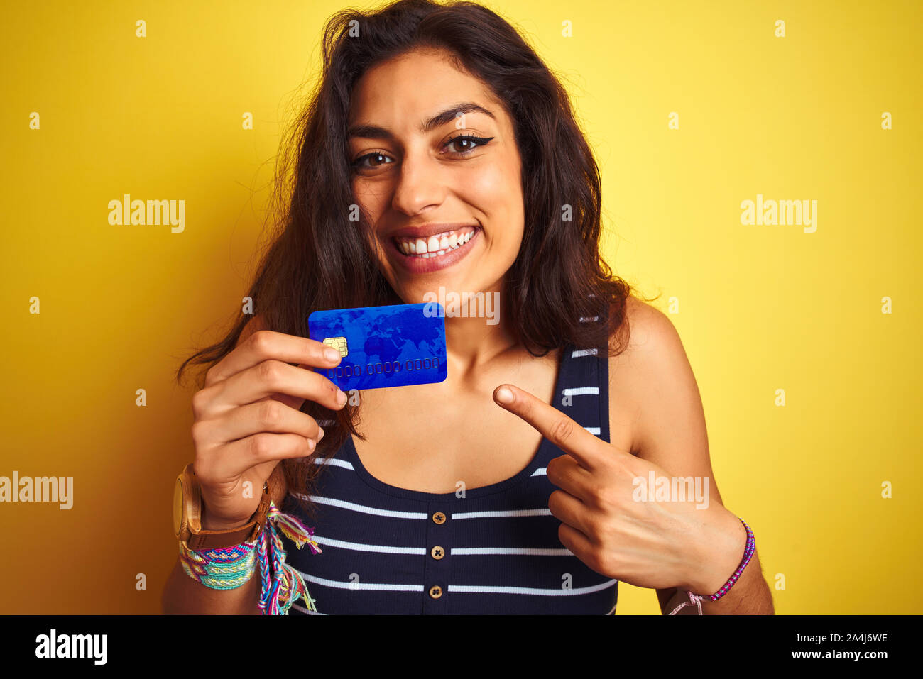 Young beautiful woman holding credit card standing over isolated yellow ...