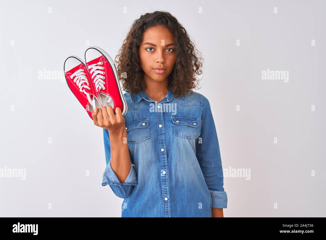 Young brazilian woman holding sneakers standing over isolated white ...