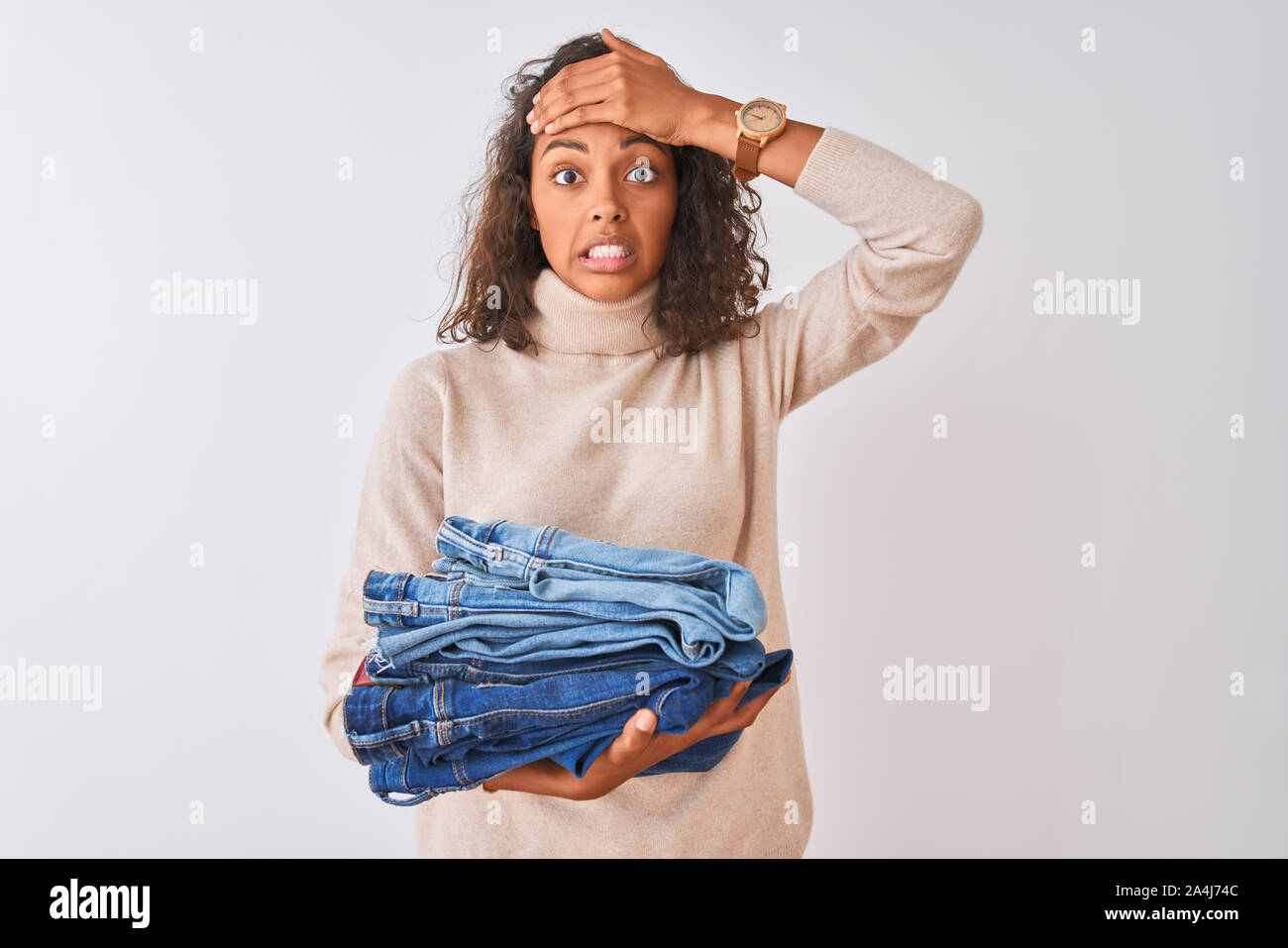 Young brazilian shopkeeper woman holding pile of jeans over isolated ...