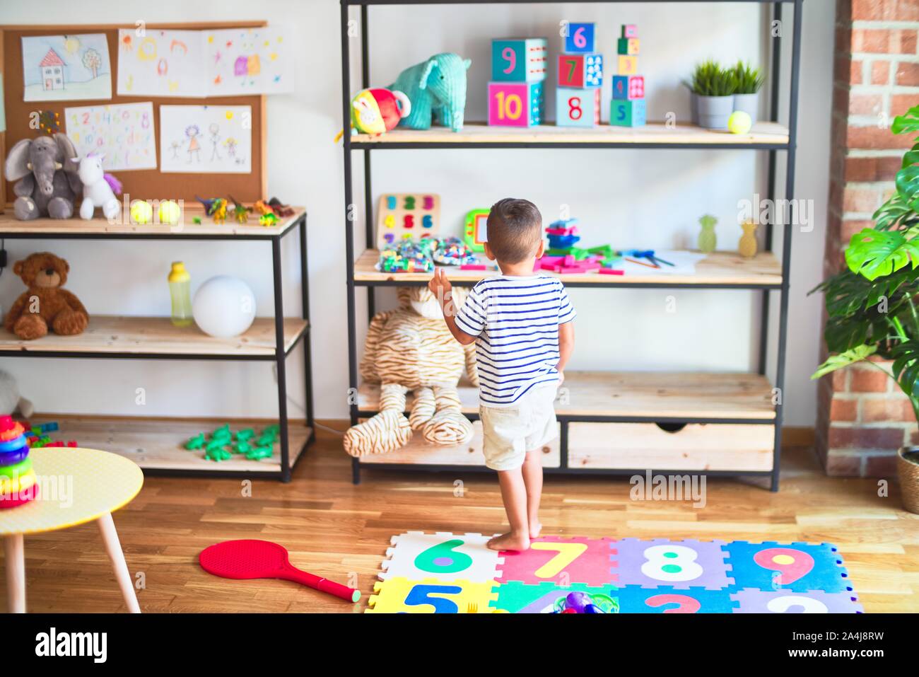 Beautiful toddler boy standing at kindergarten with lots of toys Stock ...