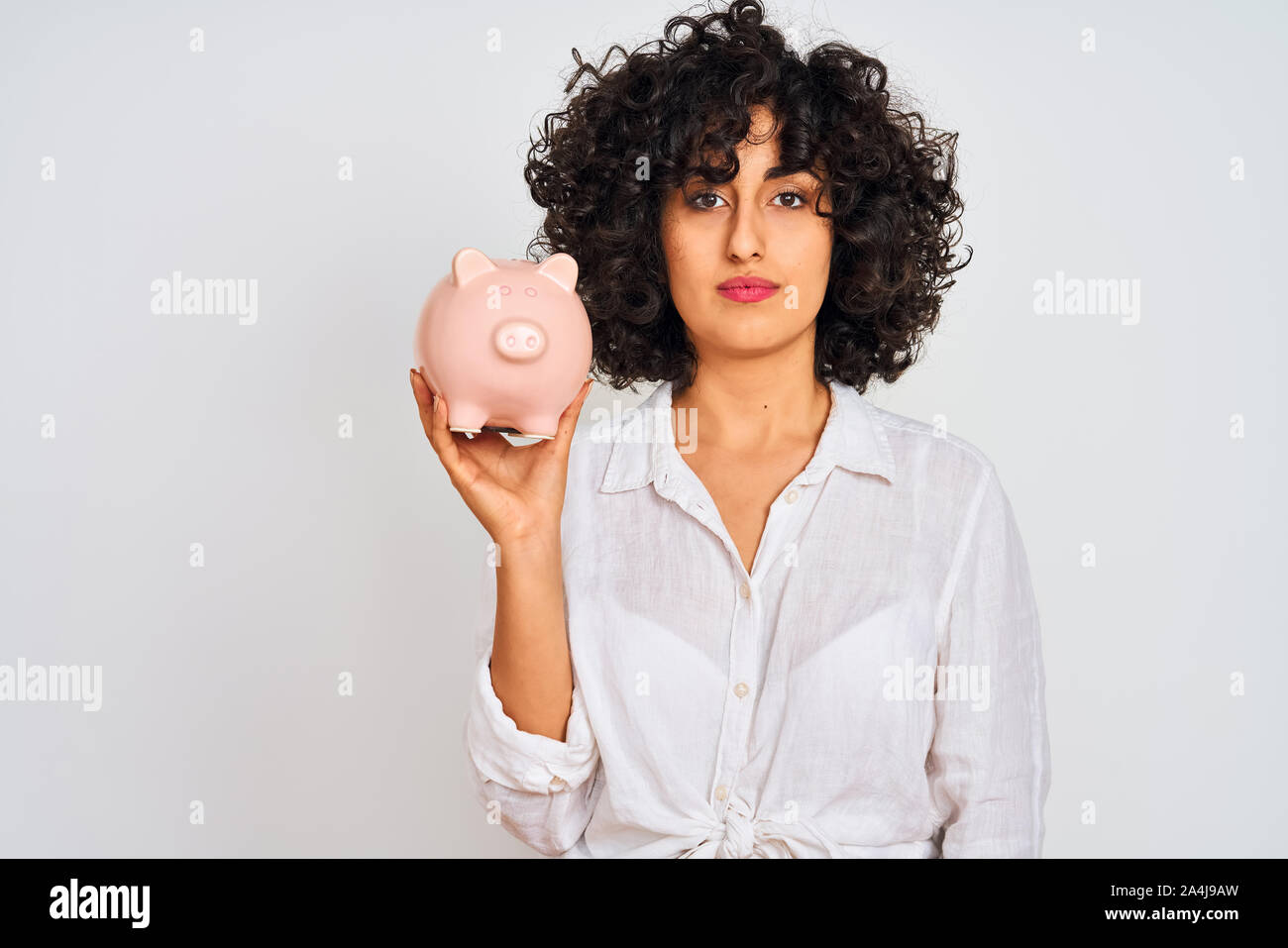 Young arab woman with curly hair holding piggy bank over isolated white ...