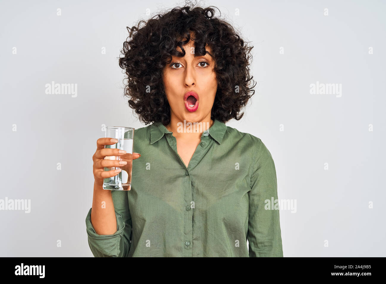 Young arab woman with curly hair holding glass of water over isolated ...