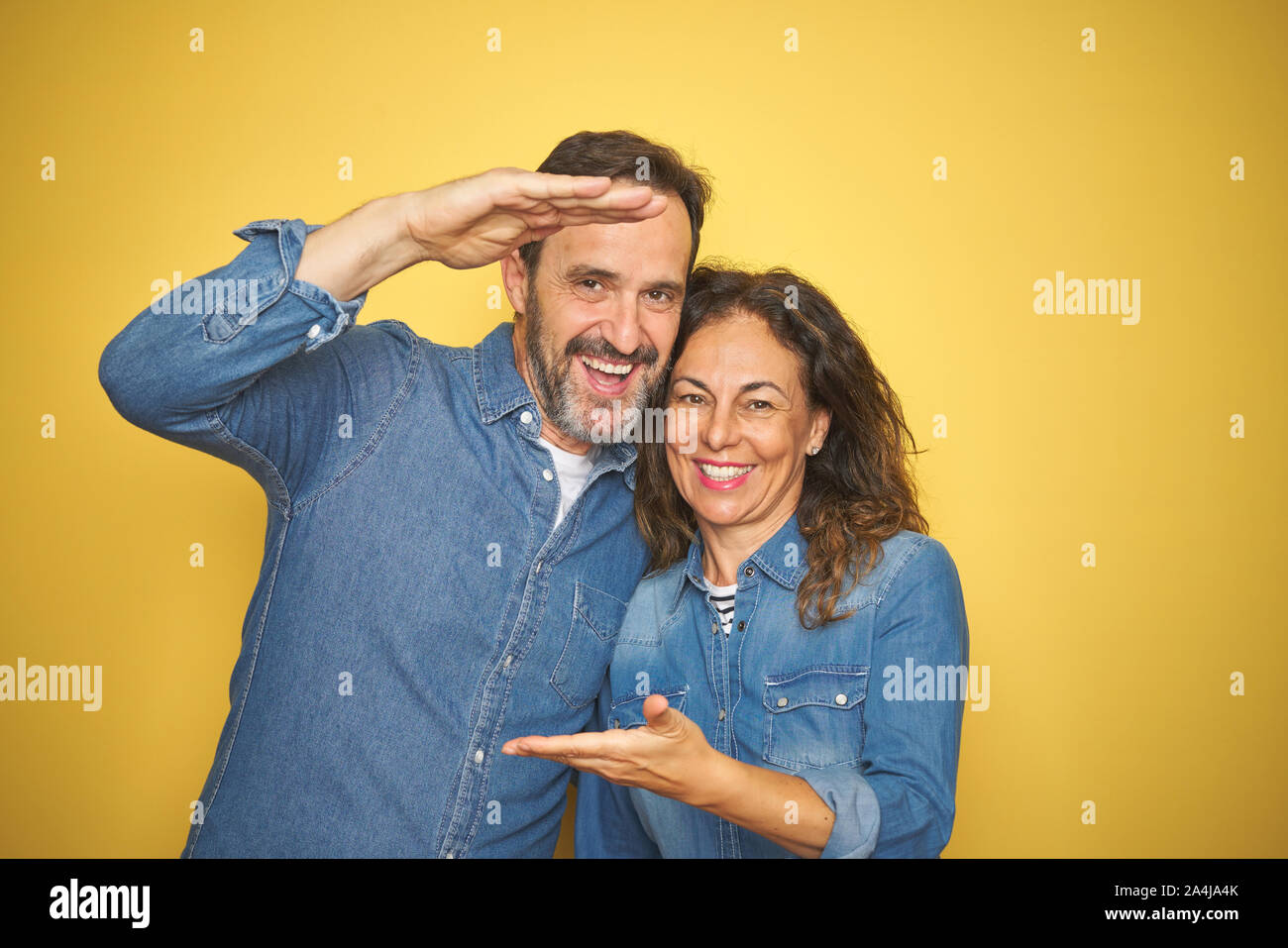 Beautiful middle age couple together standing over isolated yellow ...
